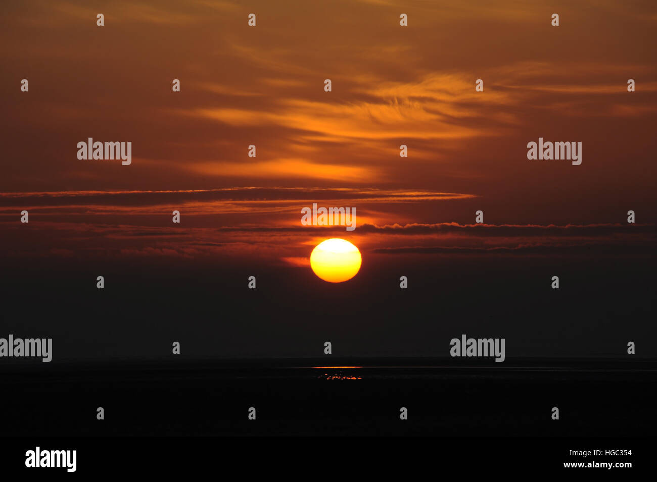 Red sky yellow sun sinking black horizon clouds above dark beach in ...