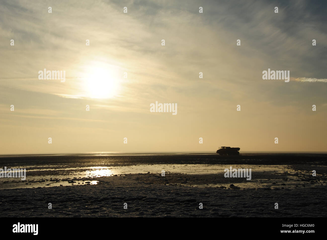 White sun sinking white clouds sky above sand-winning wagon moving sand ...