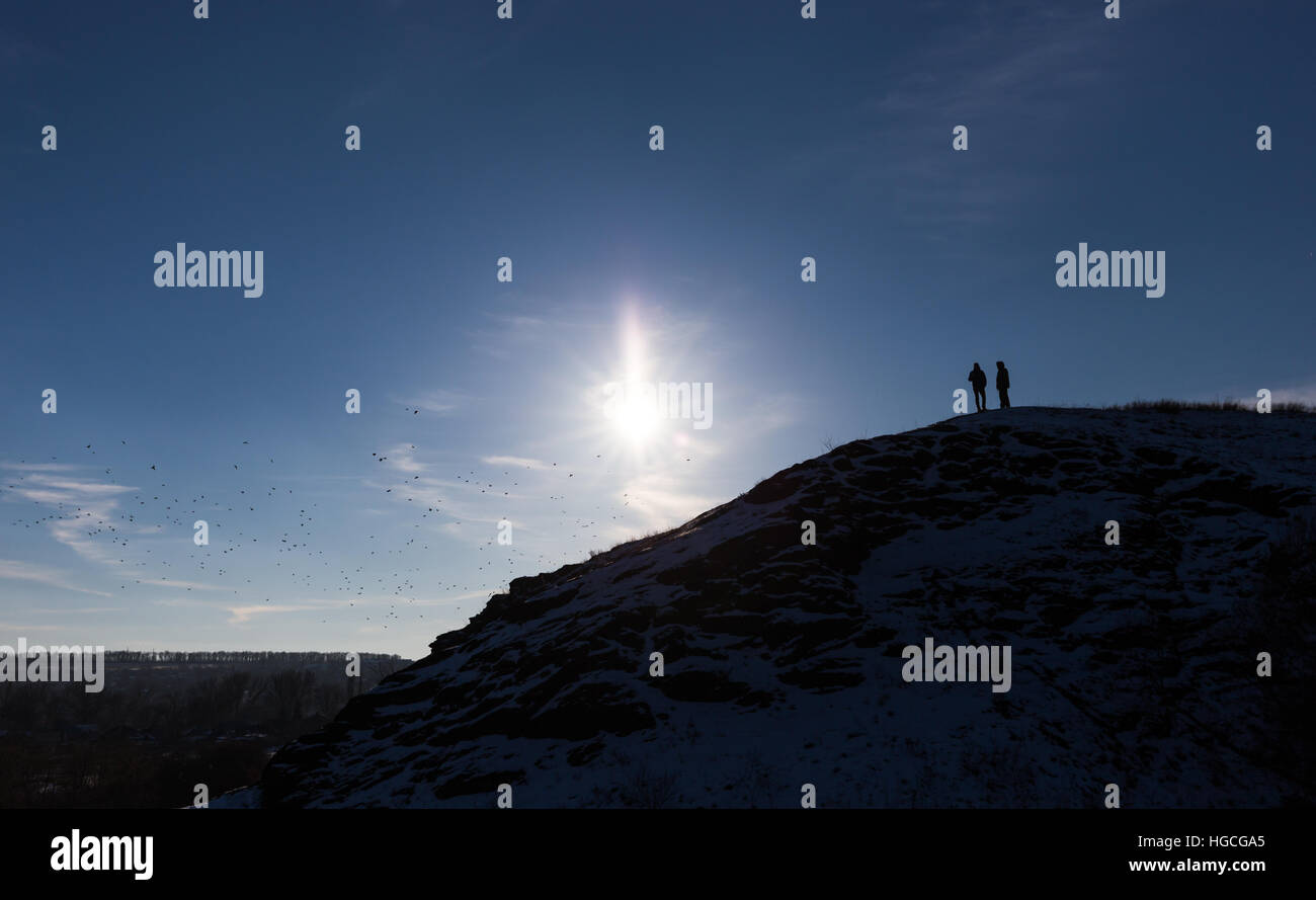 Silhouette of two men standing on the cliff, deep blue sky background ...