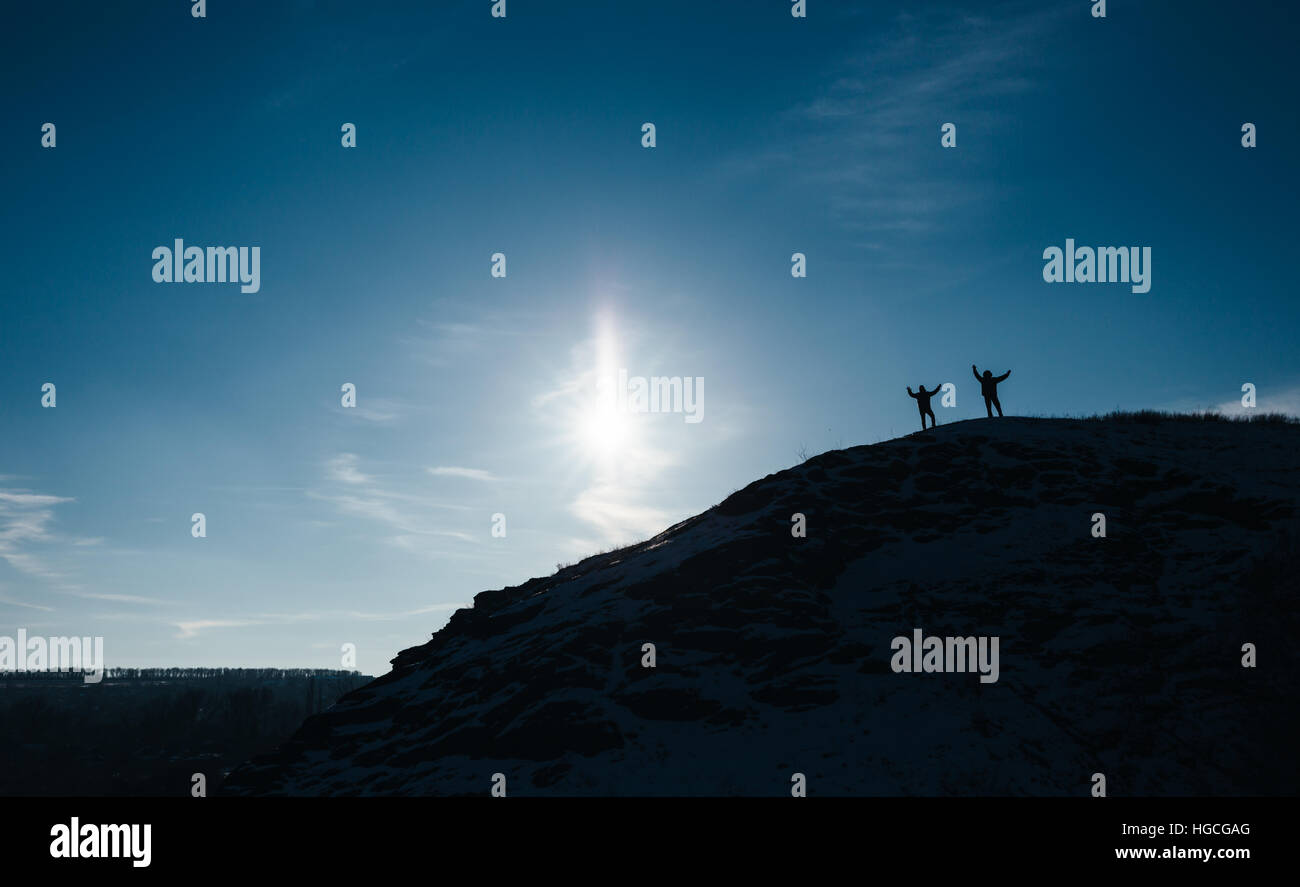 Silhouette of two men standing on the cliff, deep blue sky background ...