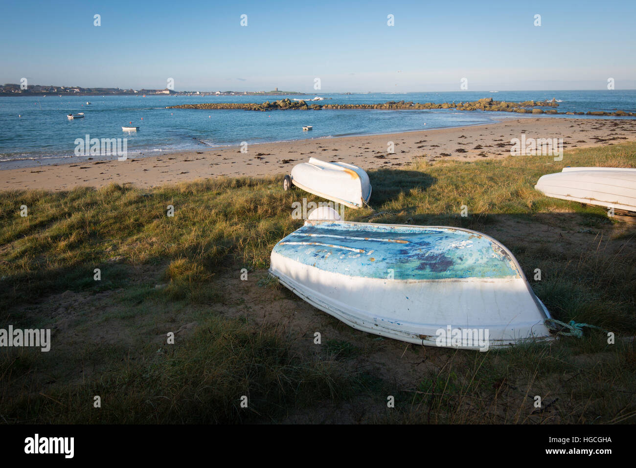 Small upturned boats on grass at top of beach, with rocks in the ...