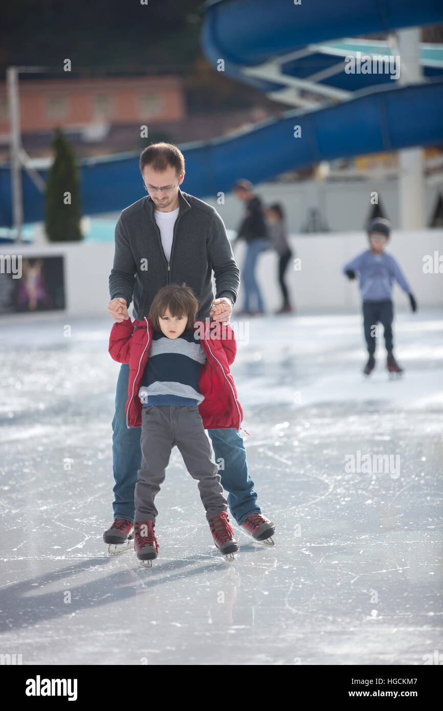 Happy excited little boy and his young father learning ice-skating ...
