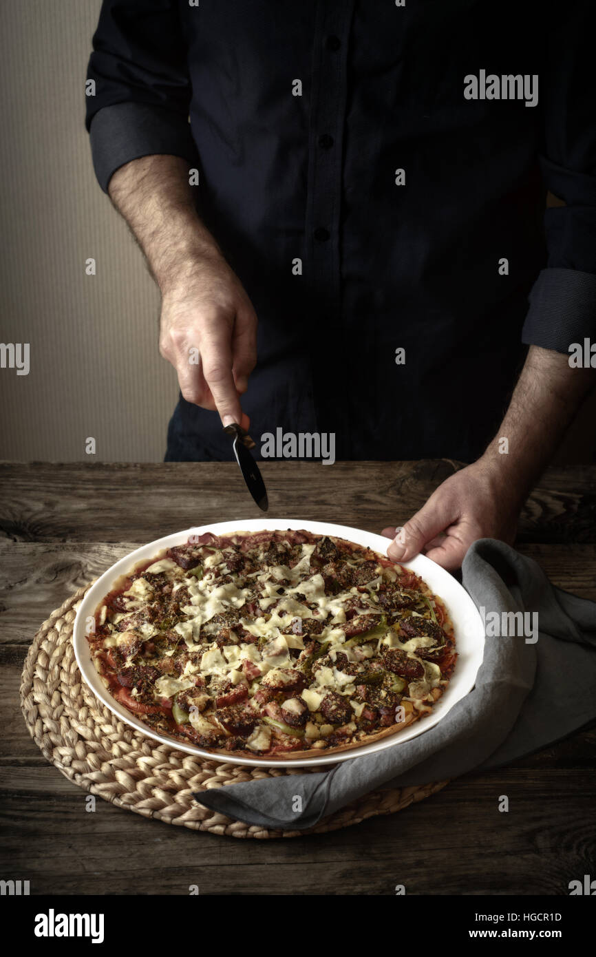 Man cuts the finished pizza on a white dish vertical Stock Photo - Alamy