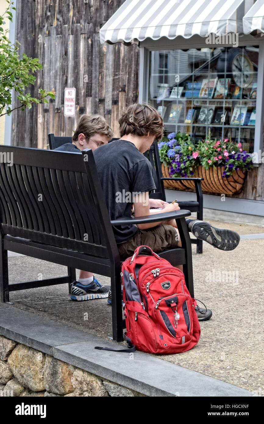 Two boys sitting on an sidewalk bench doing homework with their backs ...