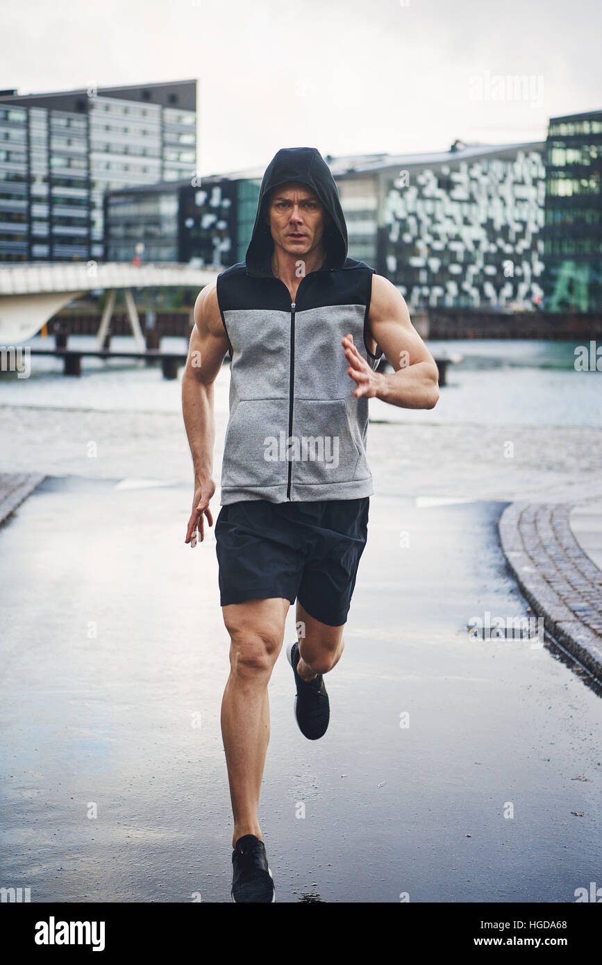 Full length shot of young man running down rainy street and looking at ...