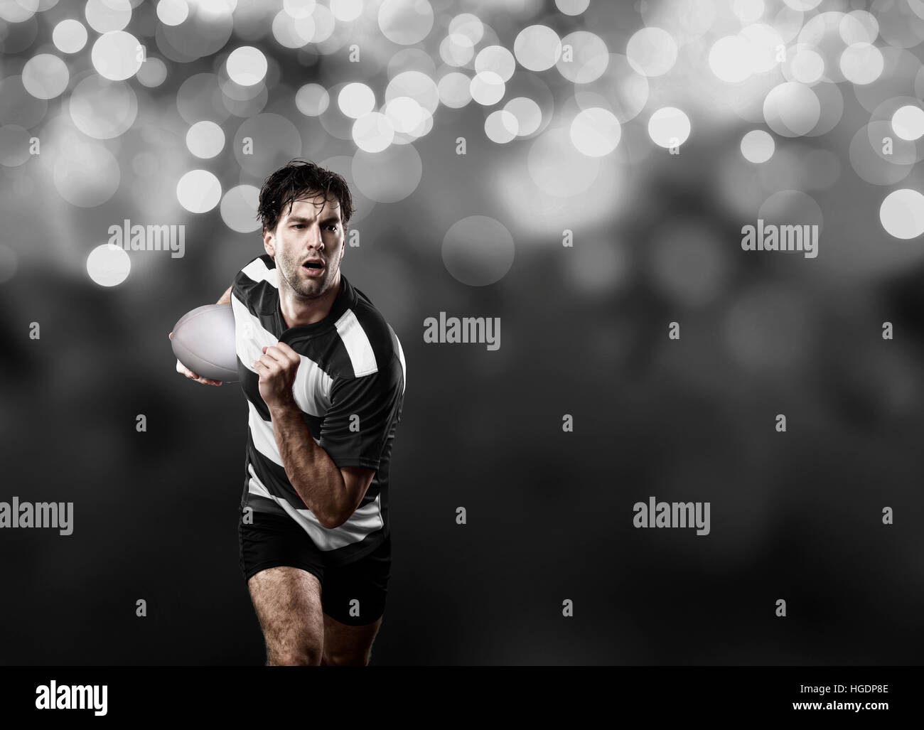 Rugby player in a black uniform running on a black lights background ...