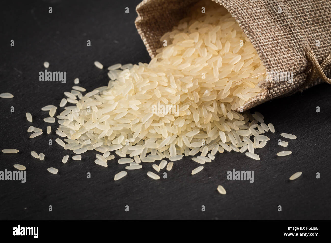 Rice in a sack and spilled on a dark background Stock Photo - Alamy