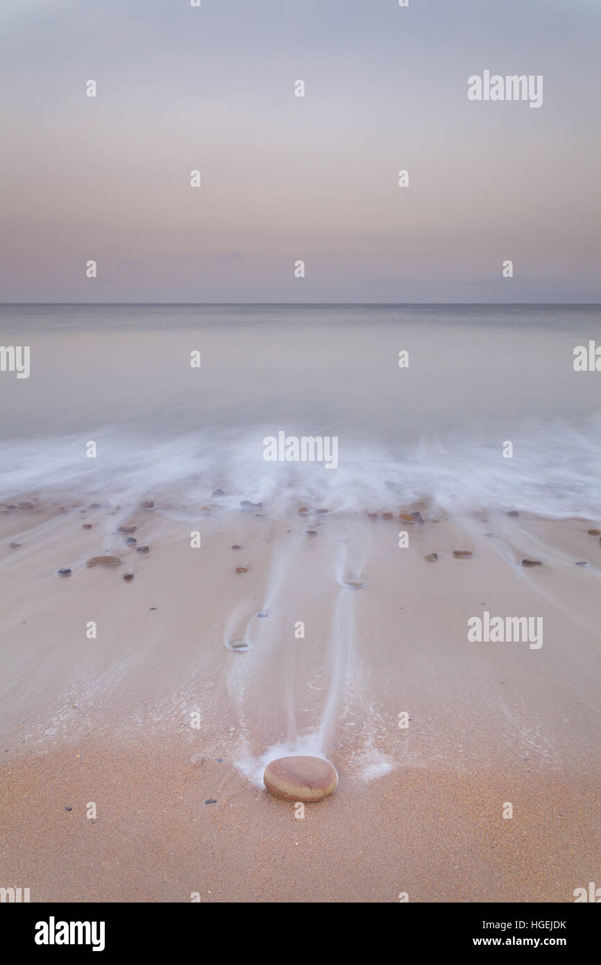 A smooth, rounded small rock with the rush of surf at high tide at ...