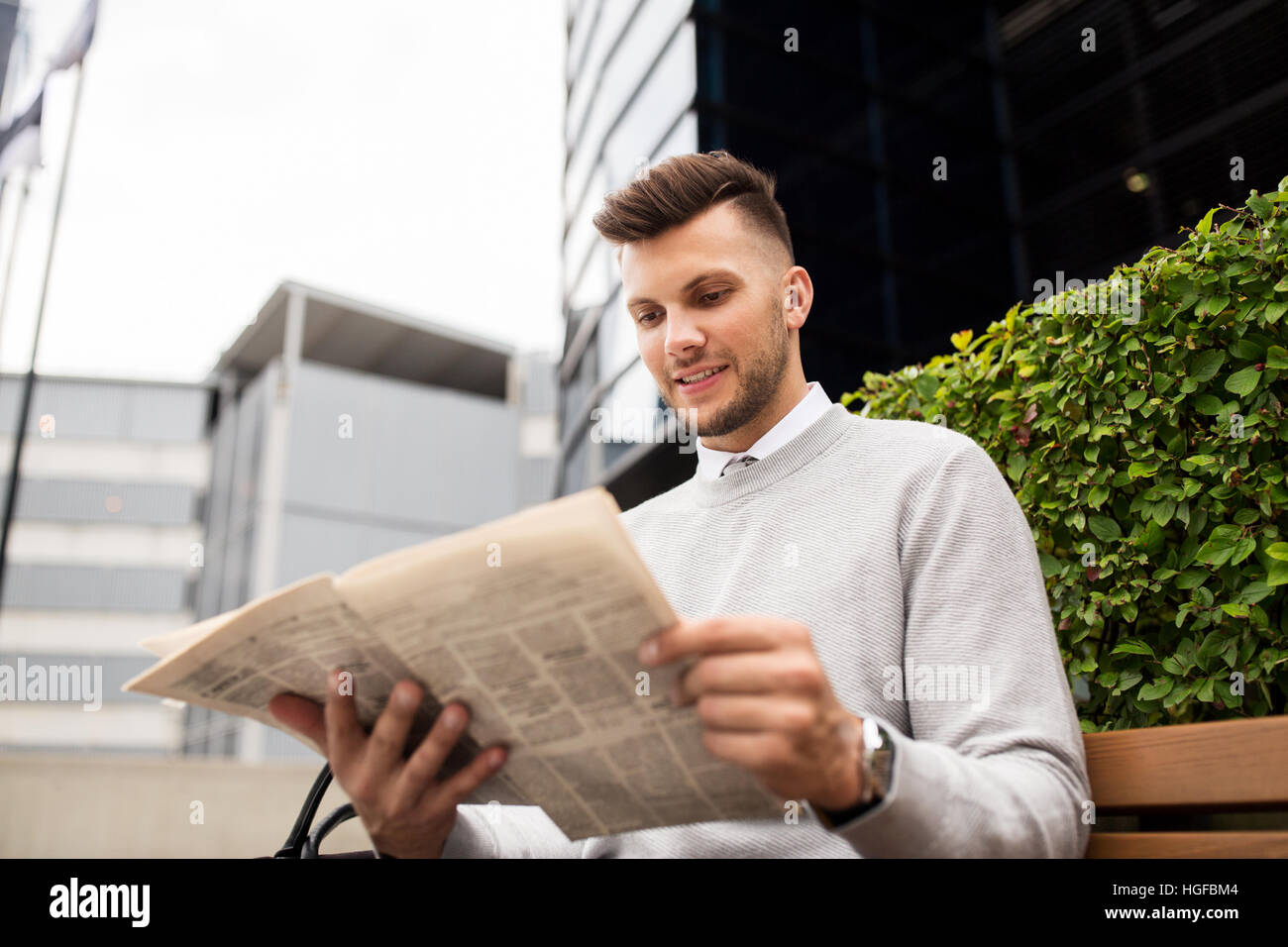 smiling man reading newspaper on city street bench Stock Photo - Alamy
