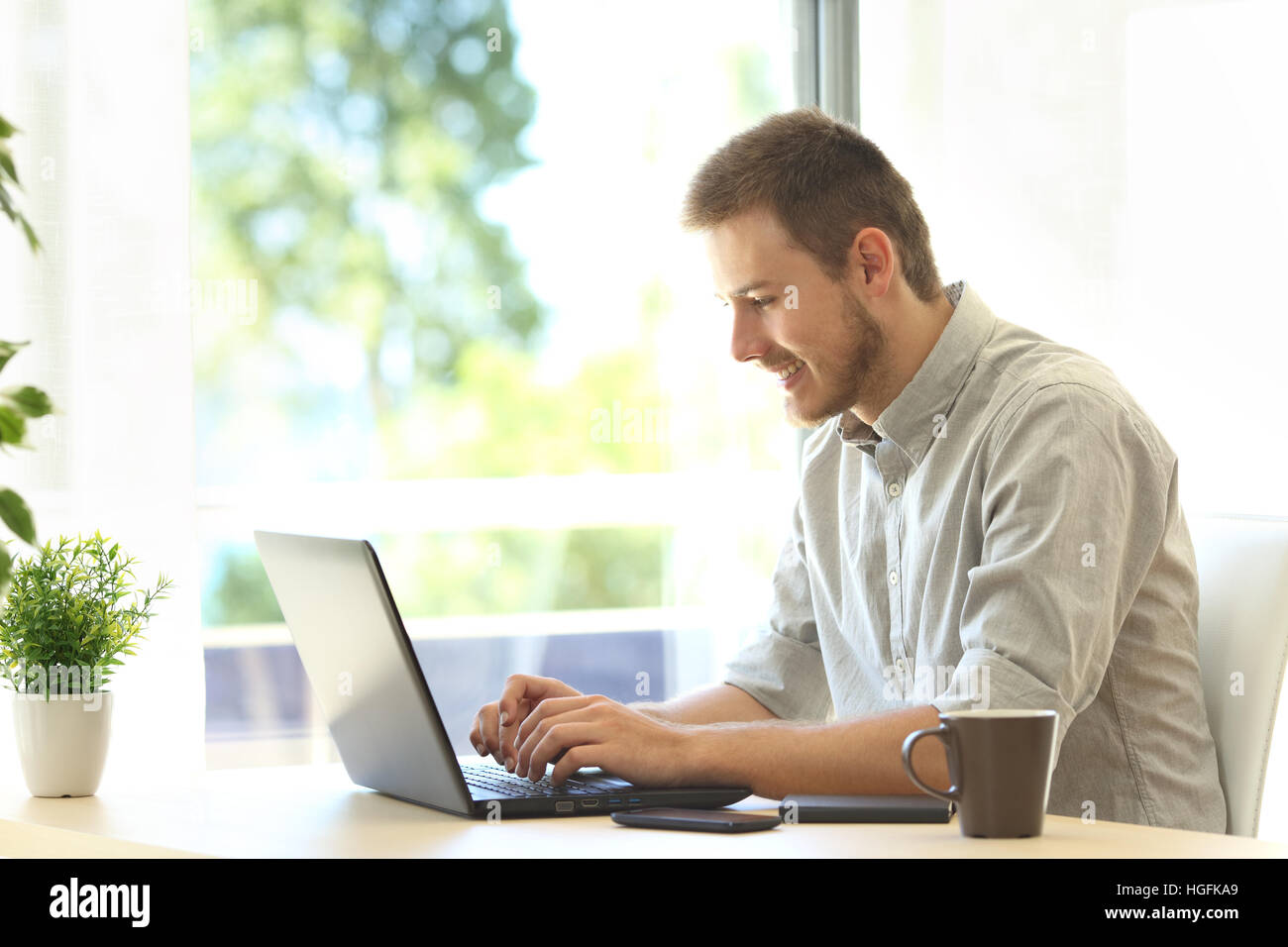 Casual writer writing with a laptop at home sitting in a table near a ...