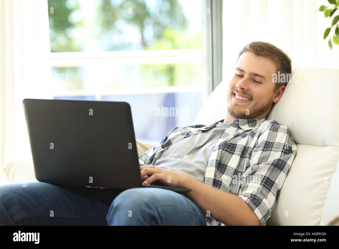 Relaxed casual man using a laptop sitting on a comfortable sofa in the ...