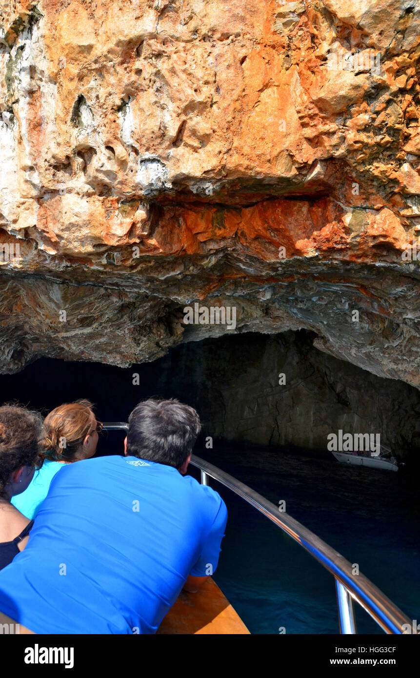 A boat of young people duck their heads as they enter the Blue Cave, on ...