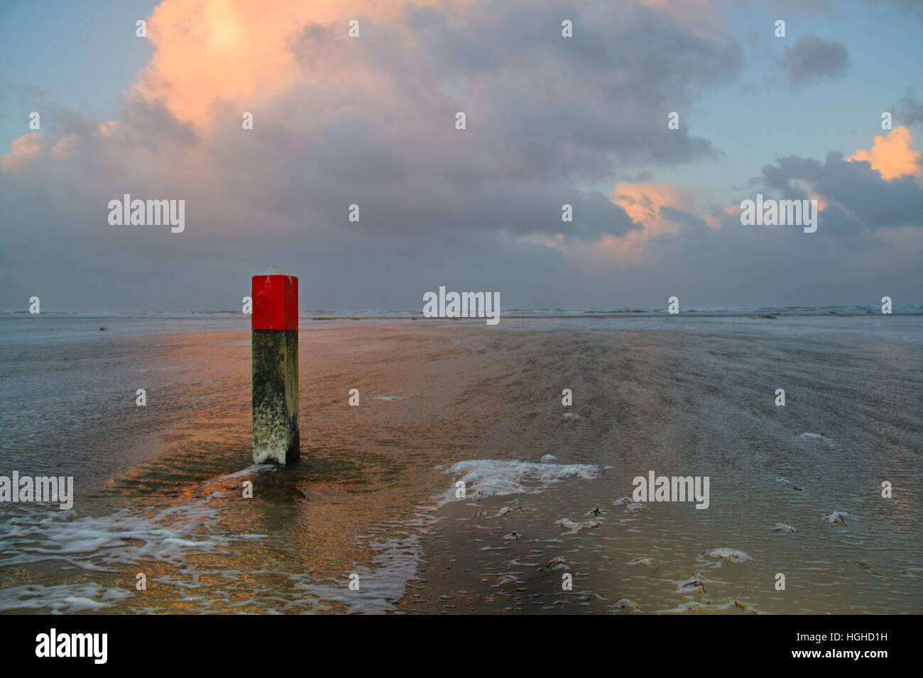 Beach with red beach pole, red clouds reflected in the sea, at sunset ...