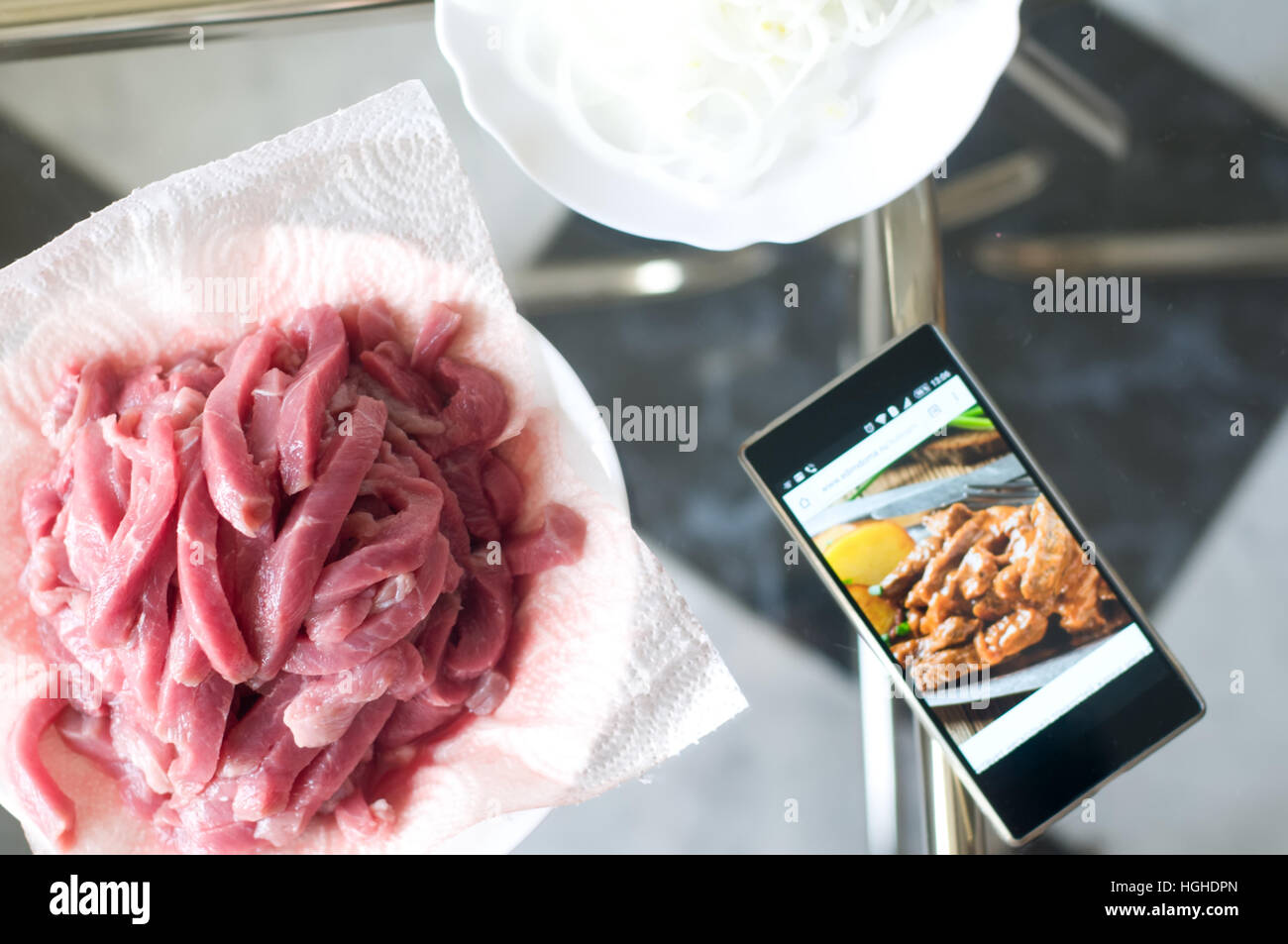 Cooking with mobile phone. Raw meat ready for beef stroganoff and onion ...