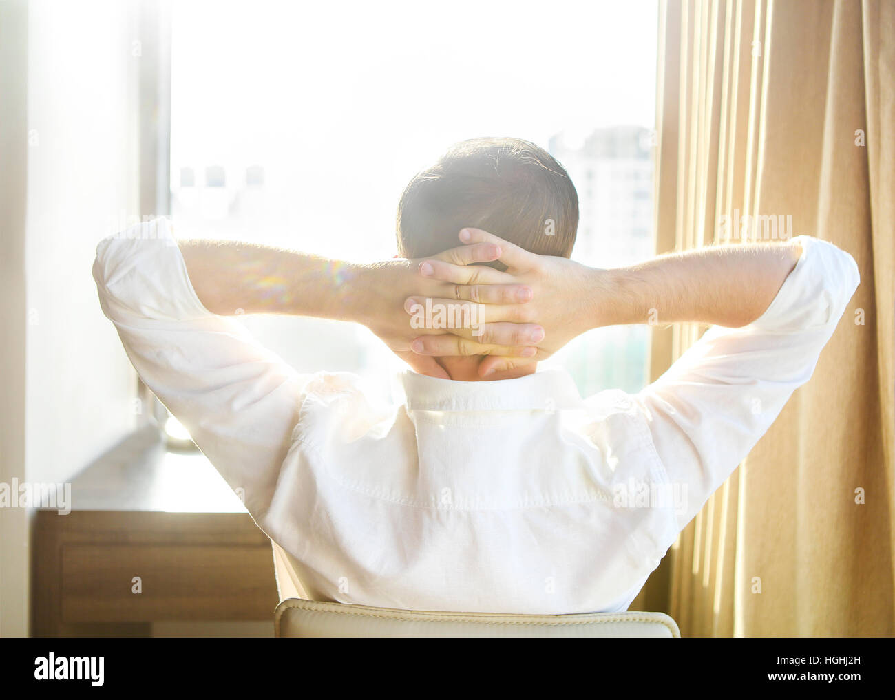 Rear view of young man relaxing on chair at home Stock Photo - Alamy