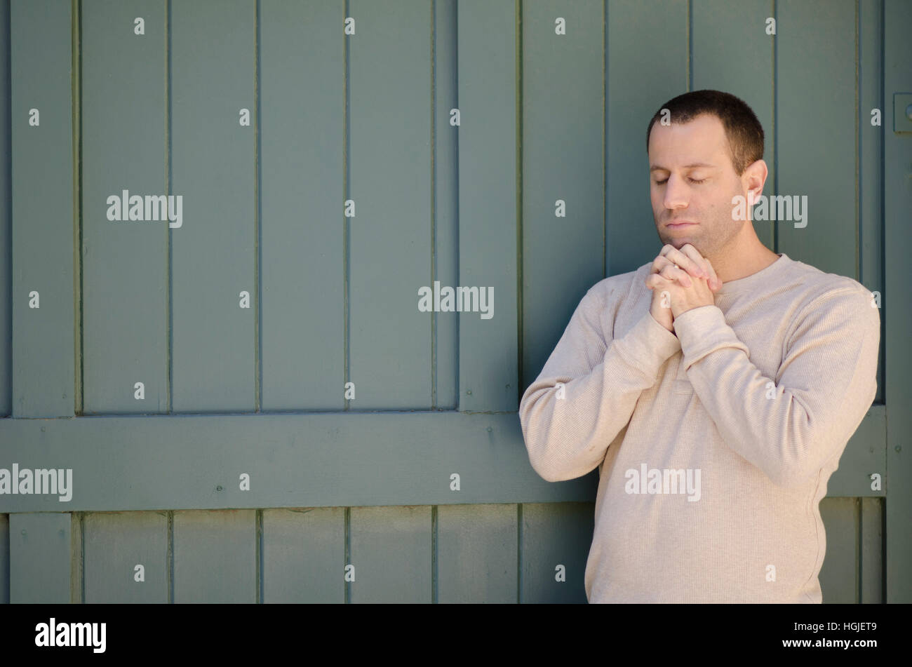 Man praying outdoors in front of a green wooden background Stock Photo ...