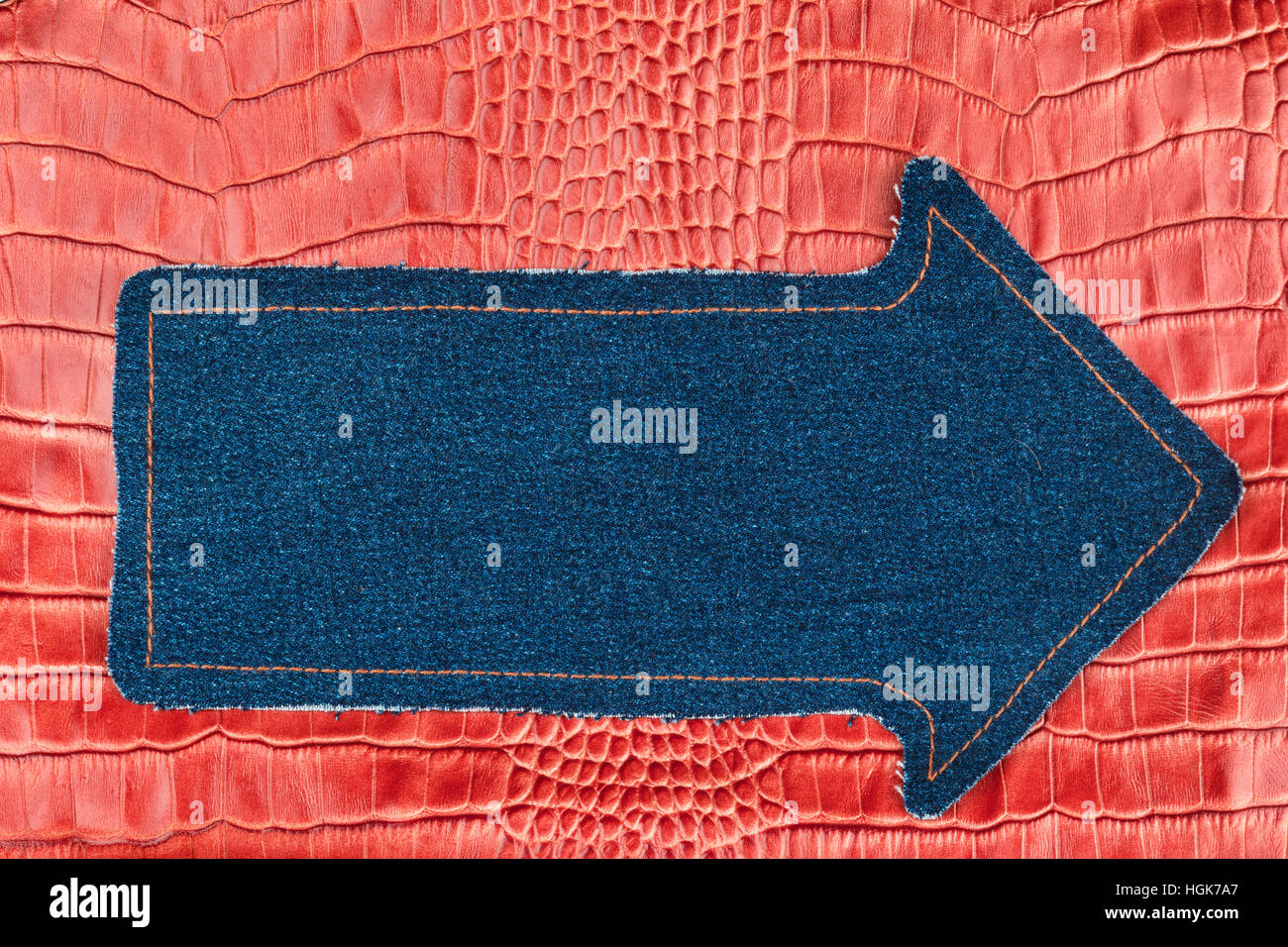 Pointer made of denim is lying on a red crocodile skin, with space for ...