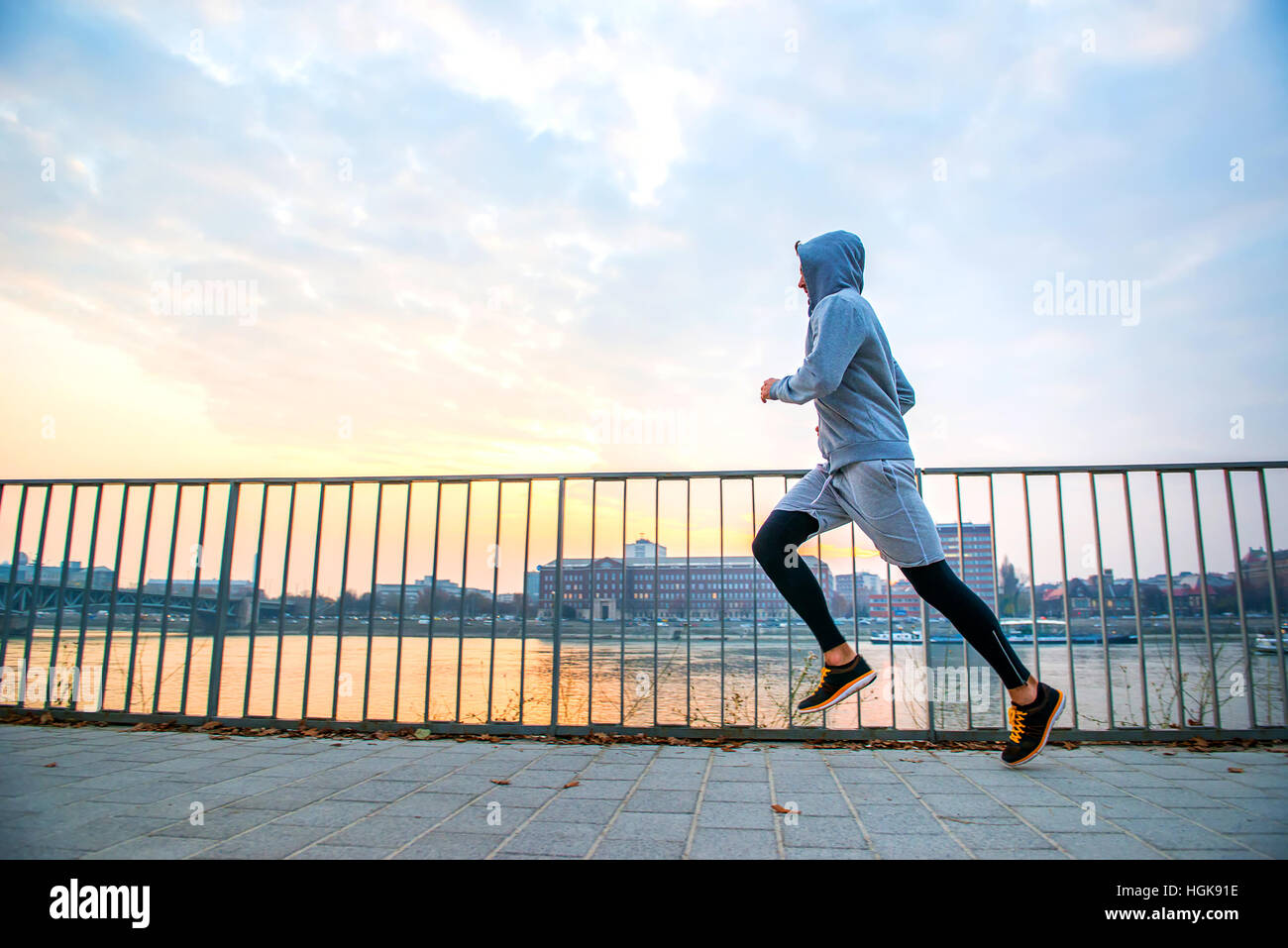 A handsome young man running in the sunset next to a fence on the ...