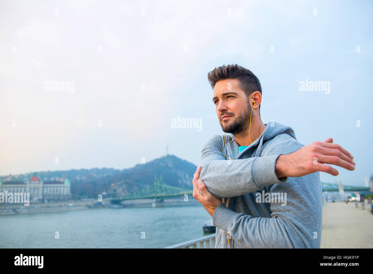 A handsome young man standing and stretching his arm at the riverside ...