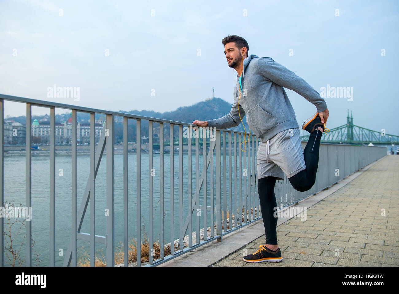 A handsome young man holding the fence and stretching his leg at the ...