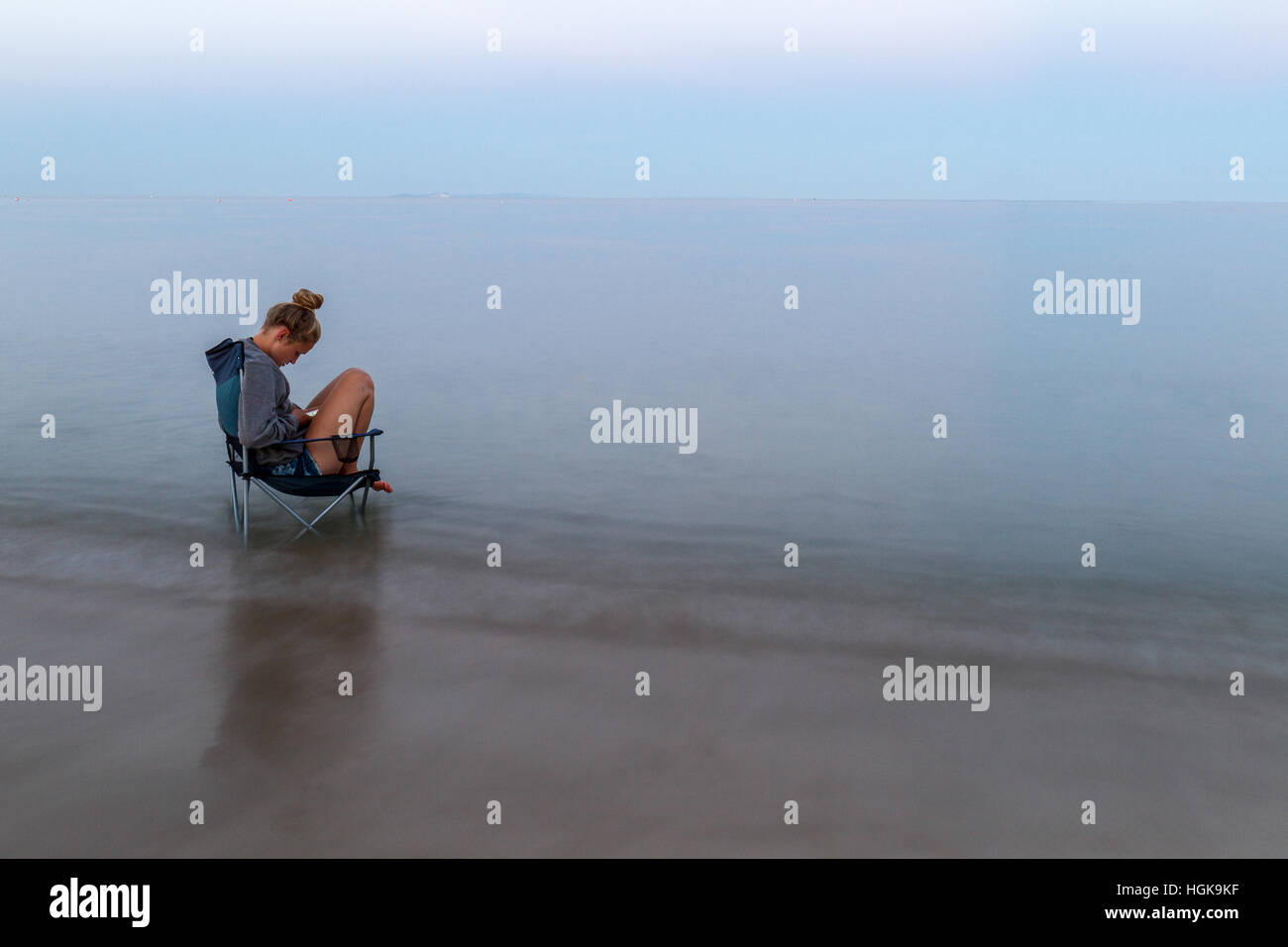 teenage girl sitting on deck chair texting in the sea Stock Photo - Alamy