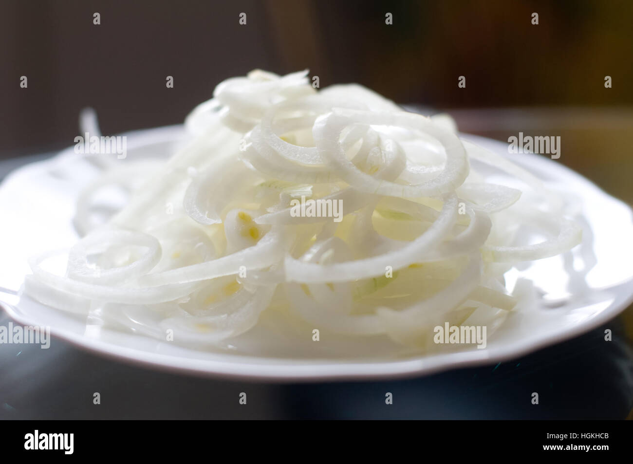 Sliced onion rings on white plate standing on glass transparent table ...