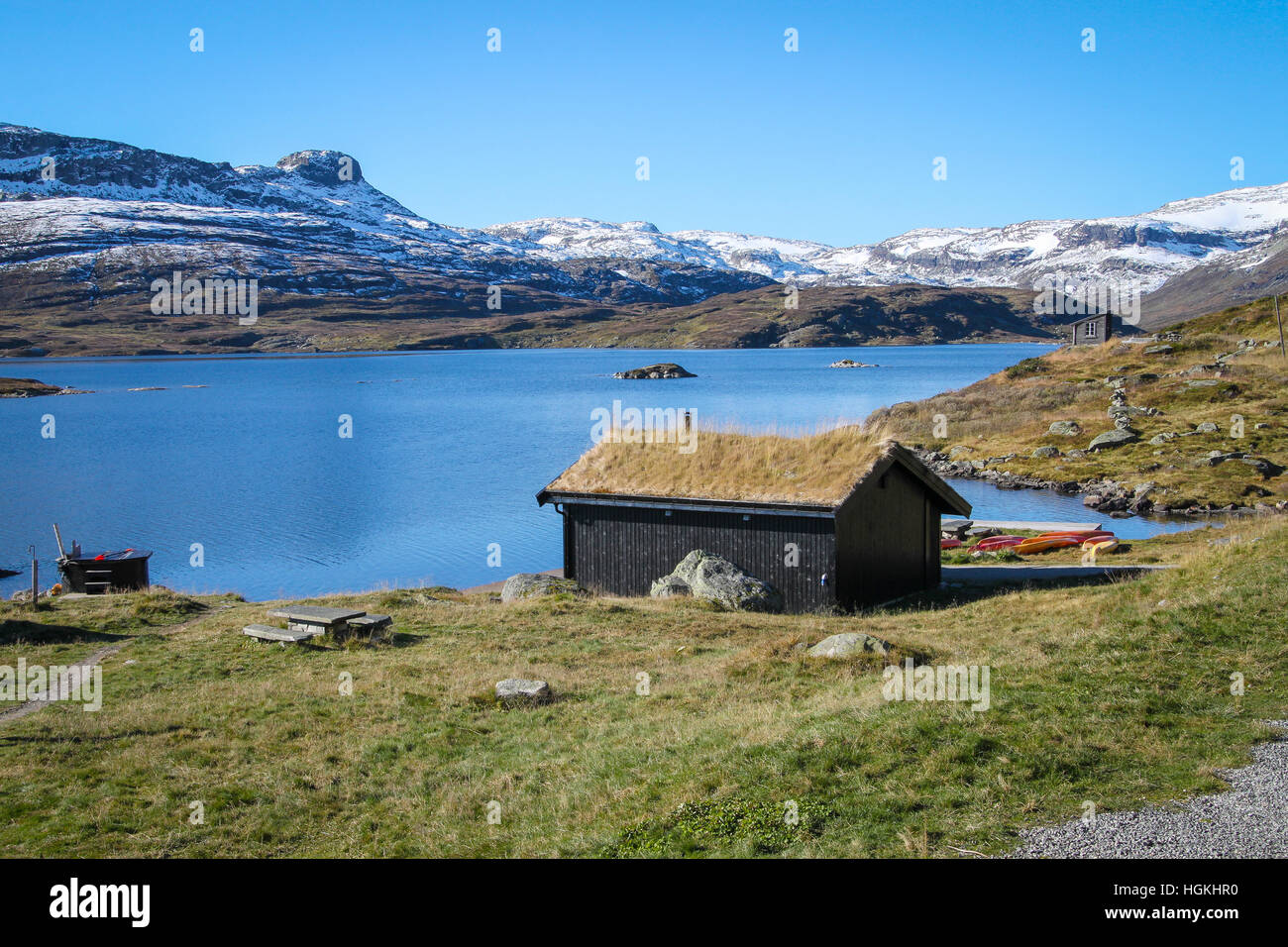 Lake with snow covered mountains and grass roofed shack with colorful ...