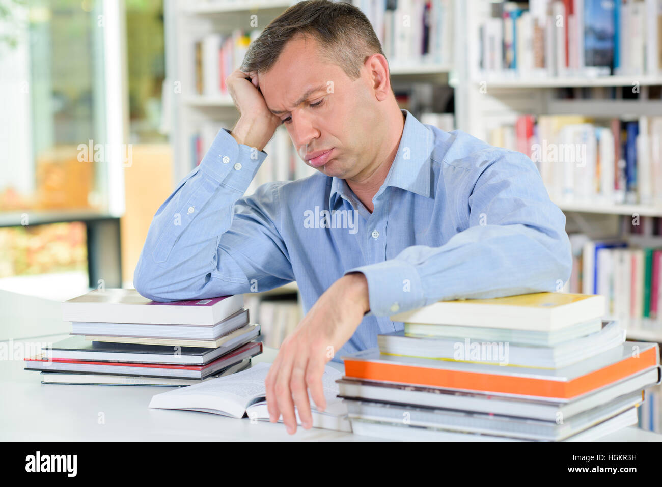 Tired man with stack of books Stock Photo - Alamy