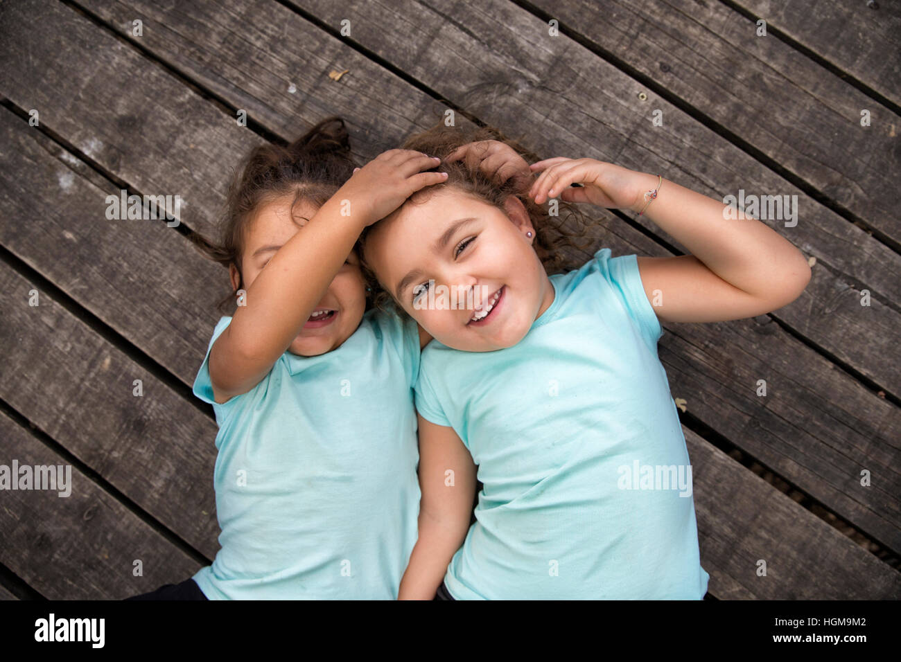 Horizontal shot of two smiling small girls holding hair lying on wooden ...