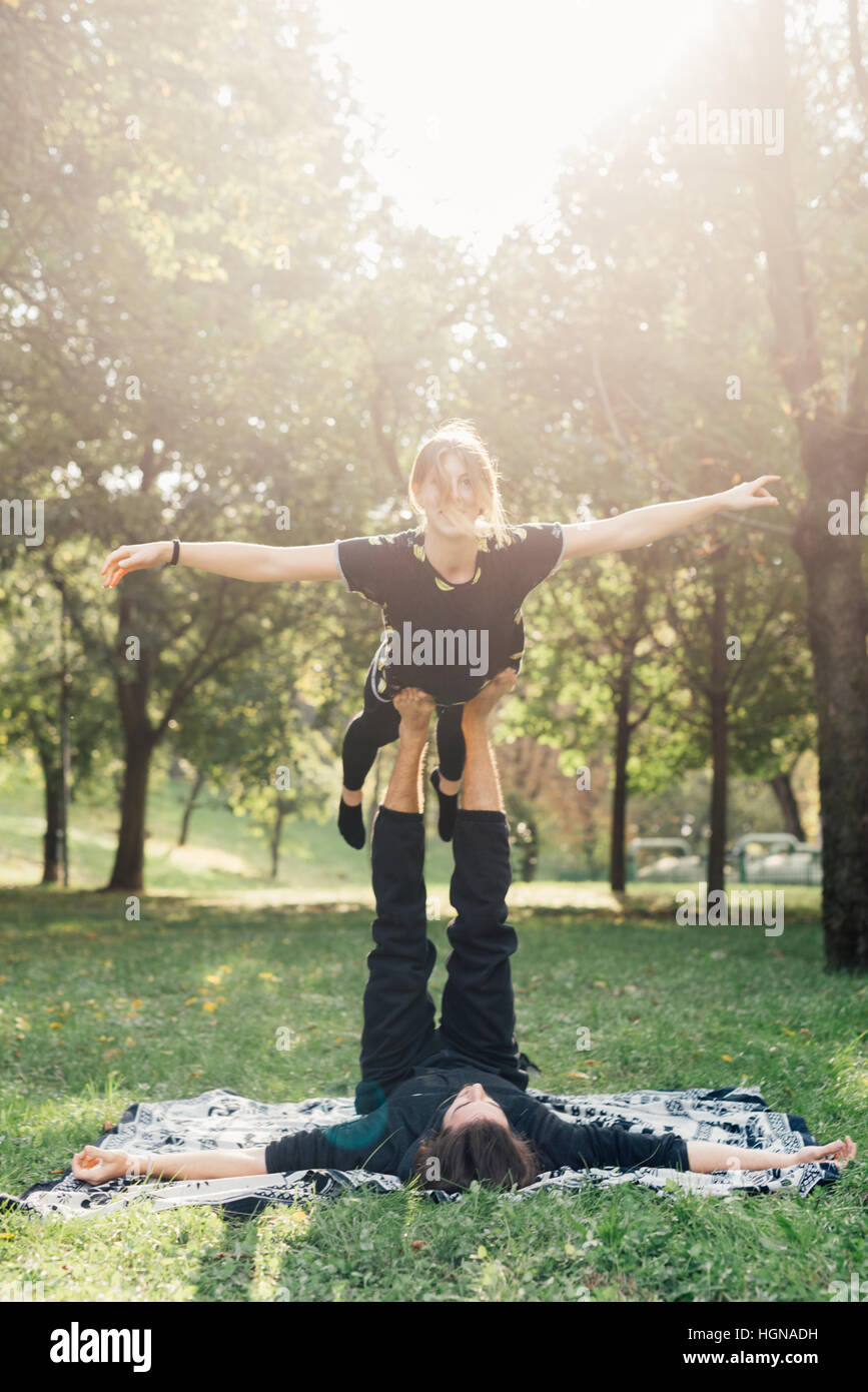 Man lifting up woman with his feet, training outdoor in a park in back ...