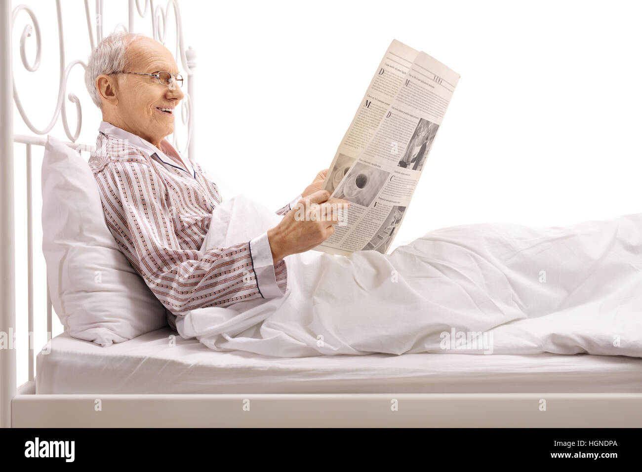 Mature man lying in bed and reading a newspaper isolated on white ...