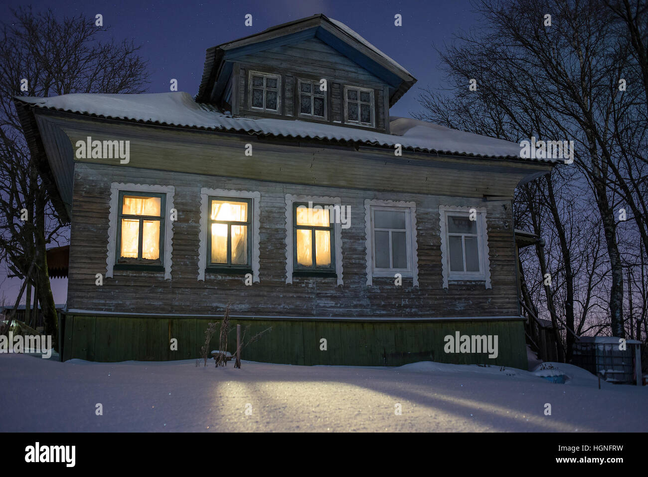 Warm light from windows ofcozy old russian village house in the bitter ...