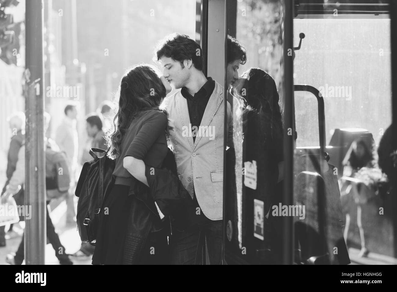 Young beautiful couple in love kissing at the bus stop in back light ...