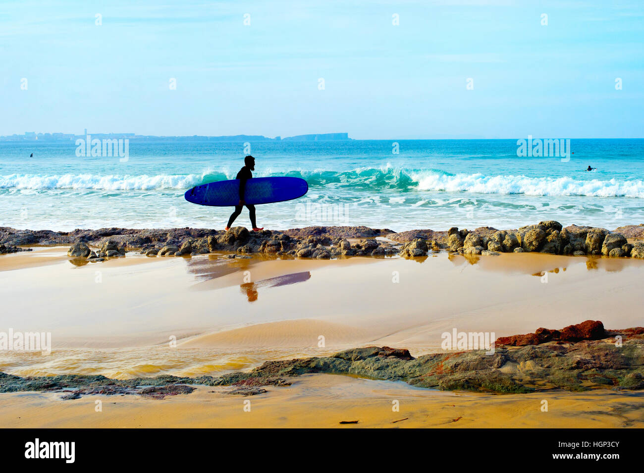 Surfer with surfboard walking on a rocky ocean beach Stock Photo - Alamy