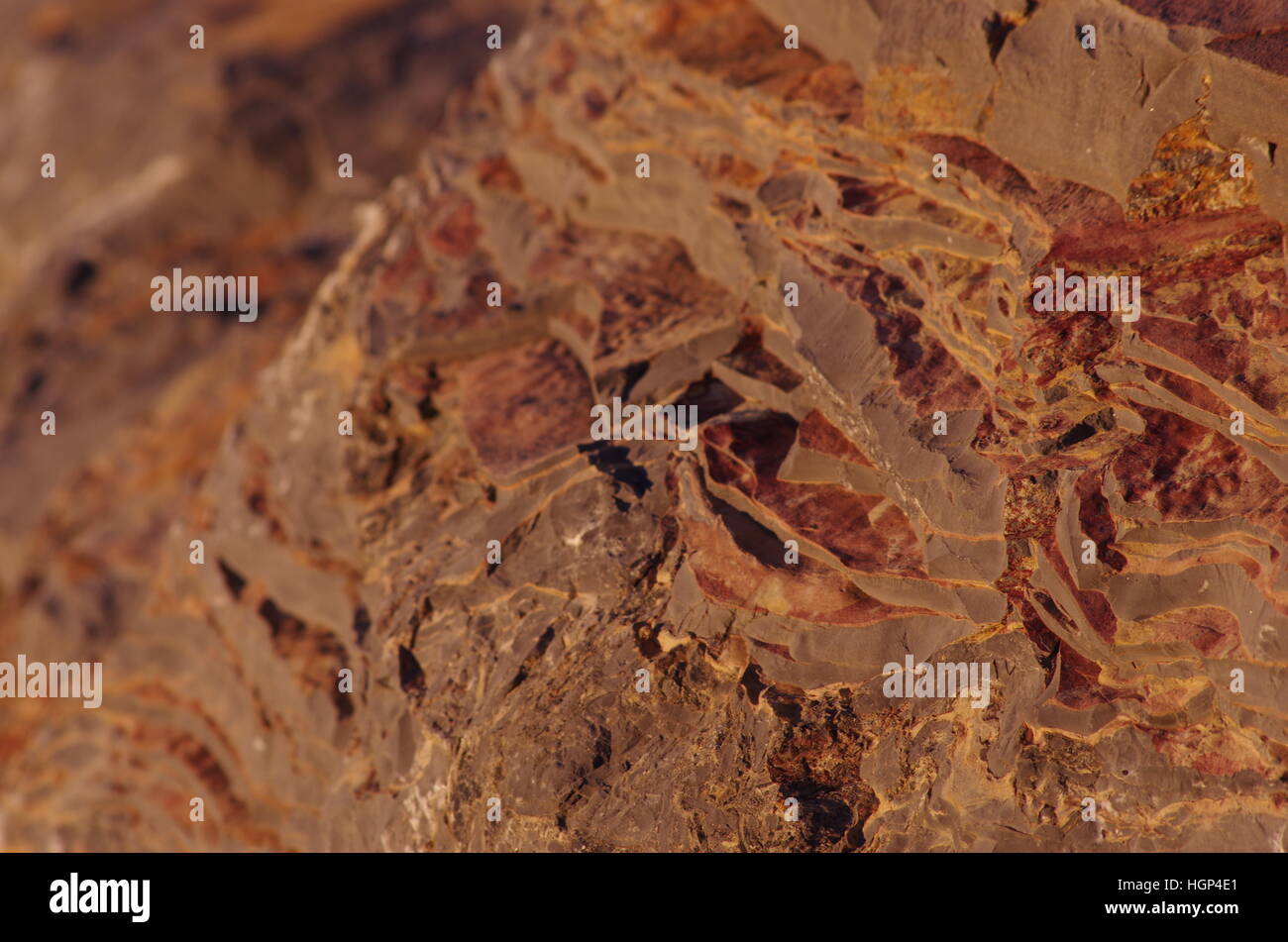 Close-up rusty red and brown chipped rock with sunlight shining on it ...