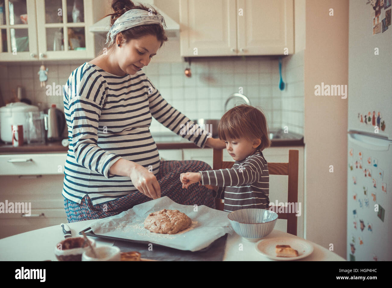 young pregnant mother with dreadlocks making bread in the kitchen with ...