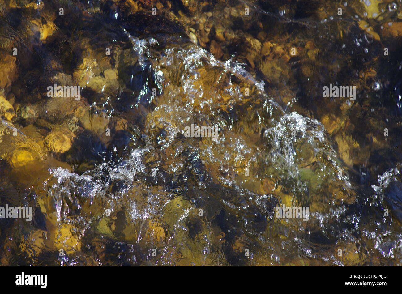 Transparent moving water splashing and rippling over copper brown rocks ...