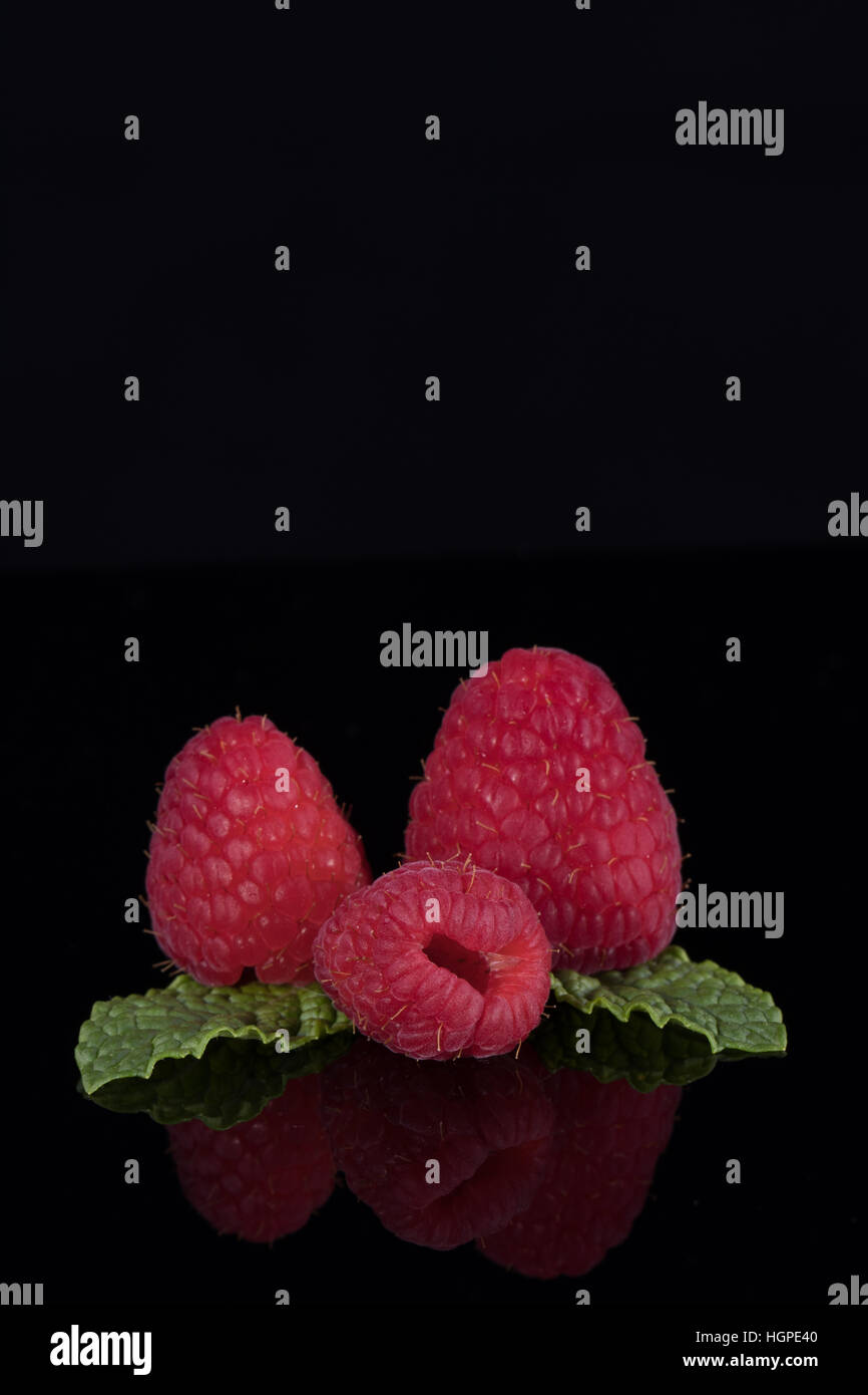 Closeup of raspberries with mint leaves on black background in portrait ...