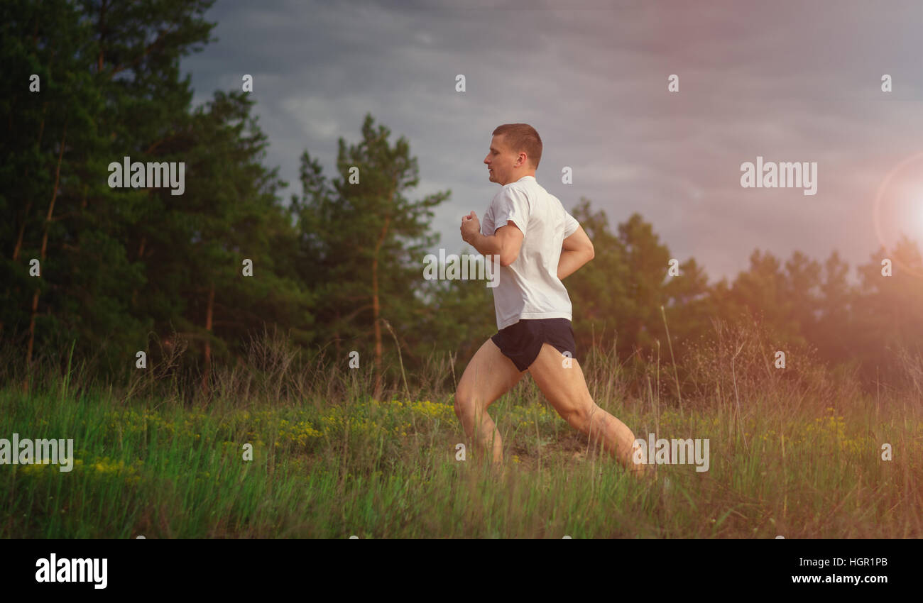 Young muscular man jogging outdoors, in the woods. Solar flare from ...