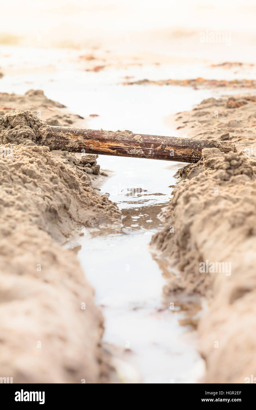 Ditch of water at the sandy beach and wooden pillar over it as a toy ...