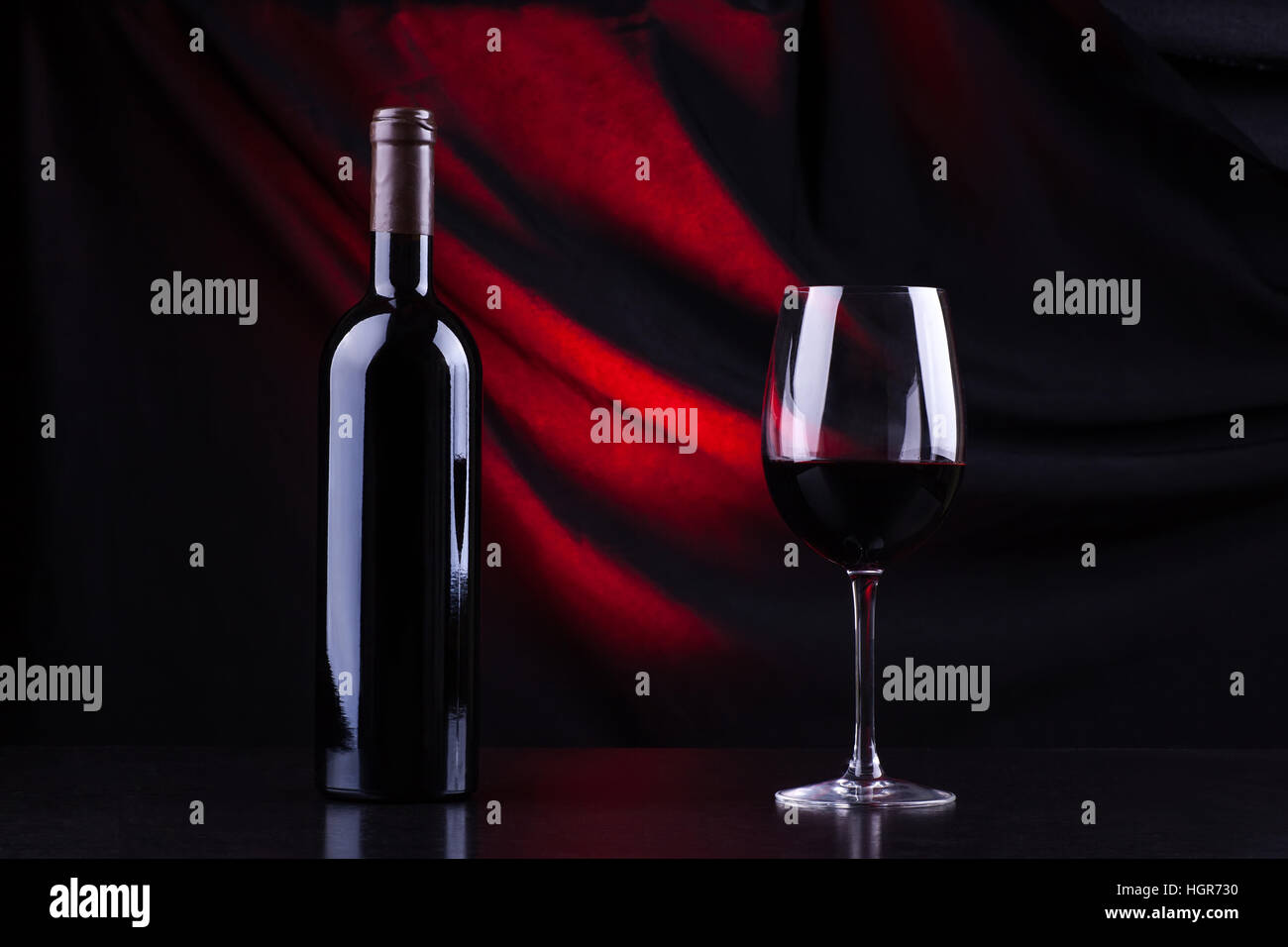 Glass and bottle of red wine with a dark background lit by a red light ...