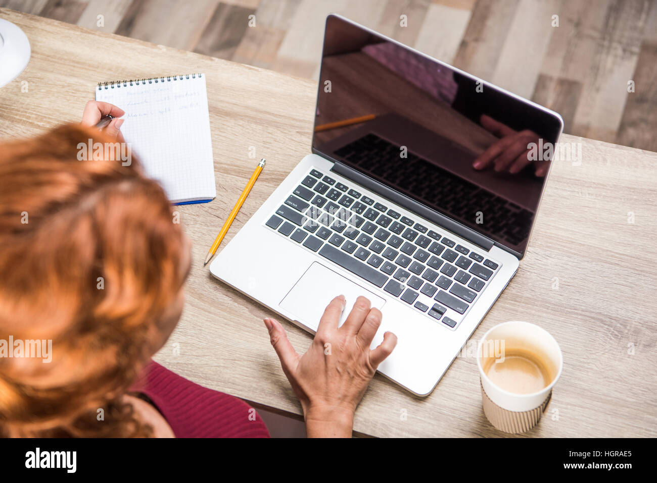 Overhead view of woman using laptop and writing in notebook Stock Photo ...