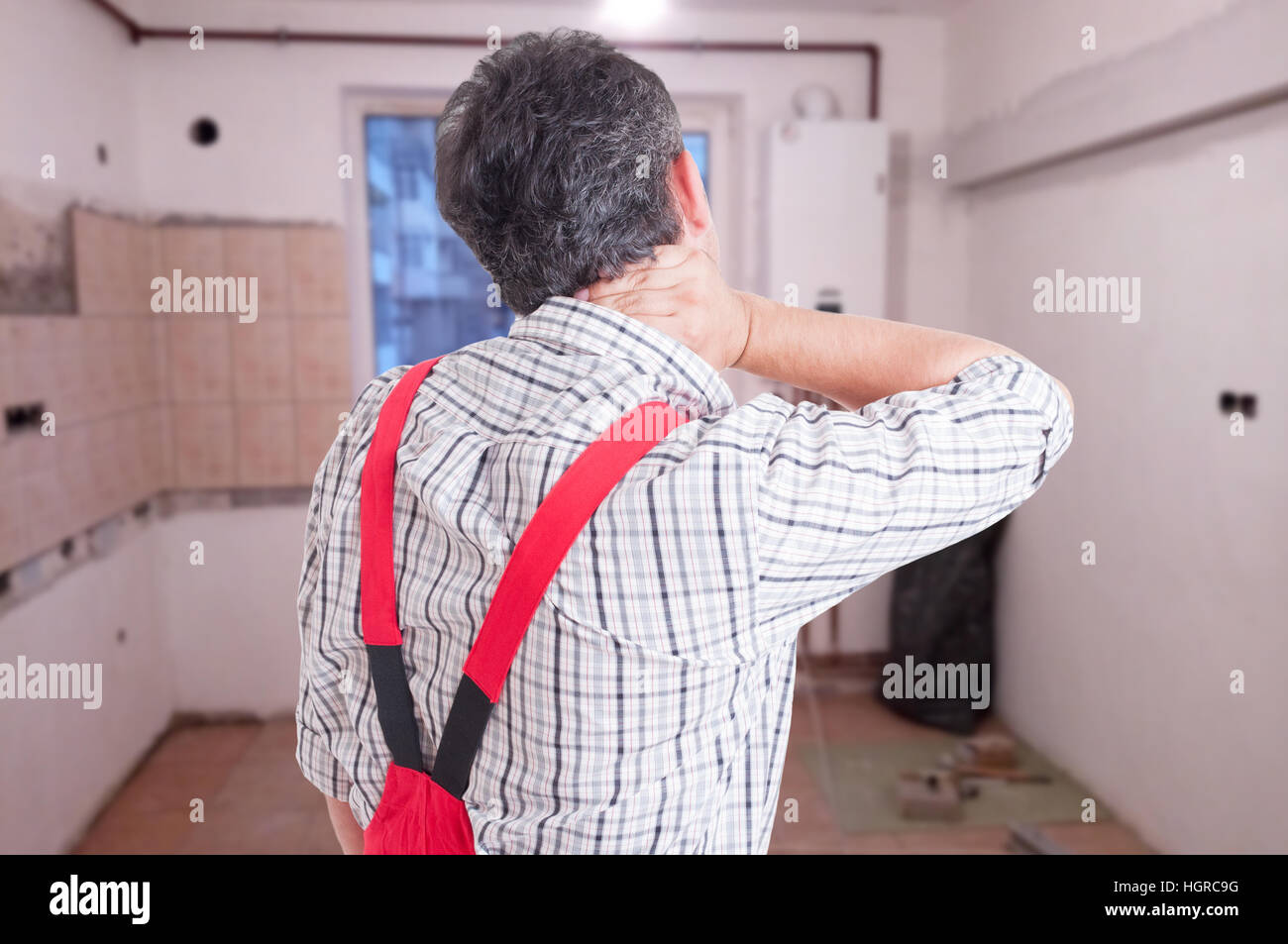 Rear view of repairman or plumber with neck pain or injury standing ...