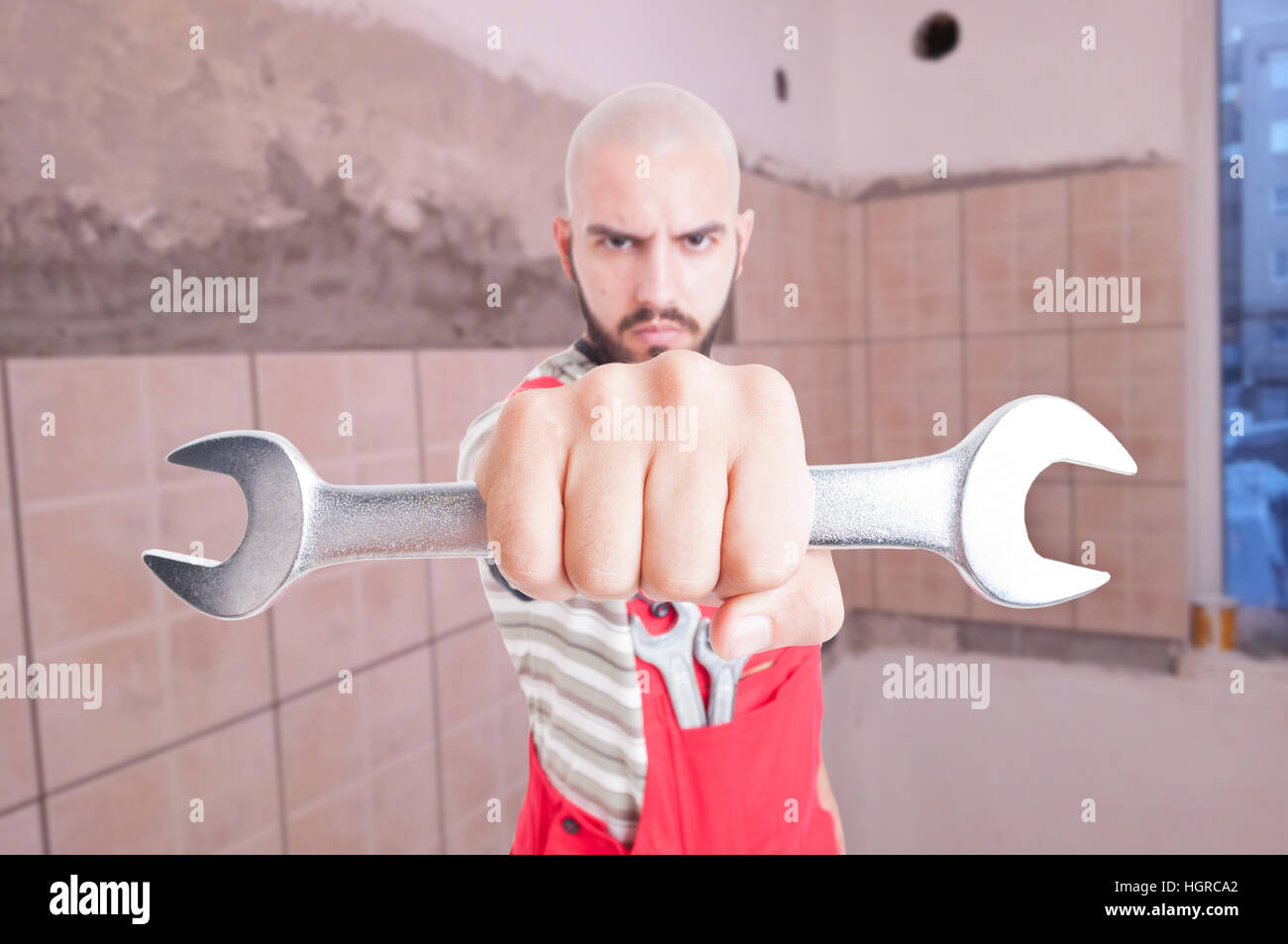 Mad or irritated plumber in work uniform holding steel wrench in ...