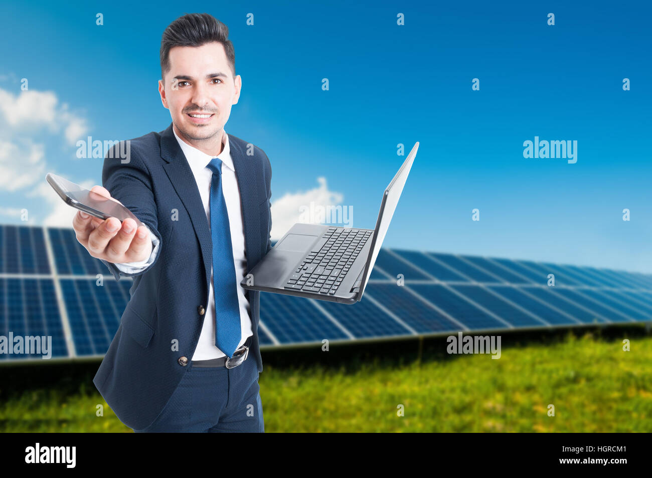 Man standing near solar panels with laptop and telephone in hand as ...