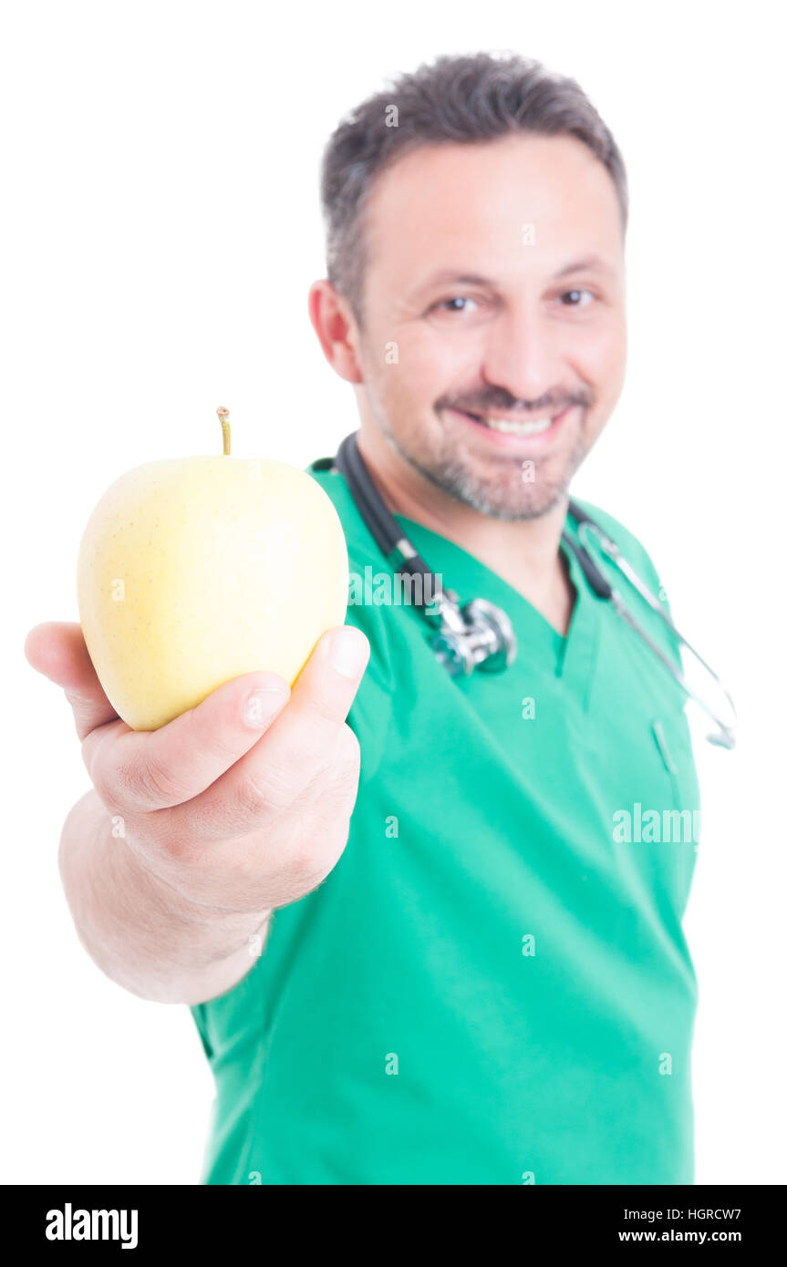 Cheerful young doctor stretching out fresh apple and smiling on white ...