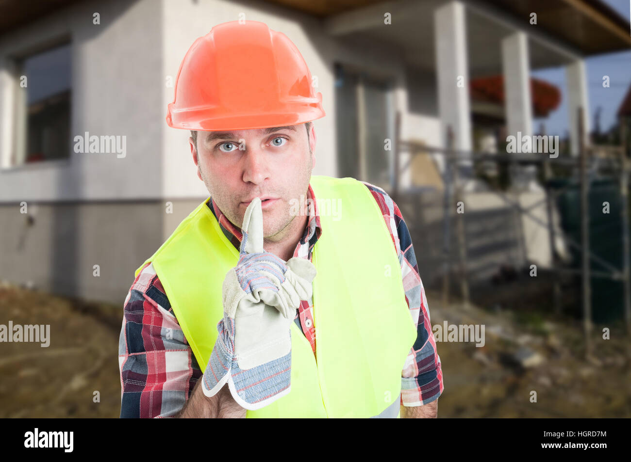 Portrait of male engineer doing quite or shush gesture in front of ...