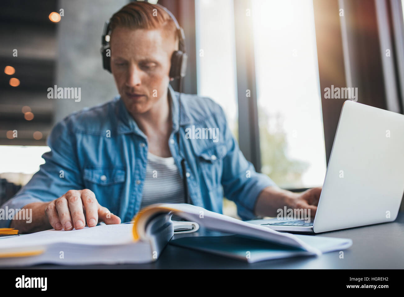 Male student sitting at table with books and laptop. Young man studying ...