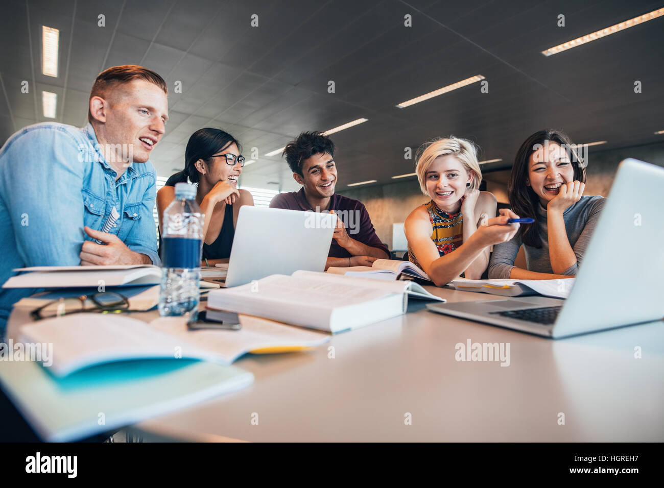 university students sitting together at table with books and looking at ...