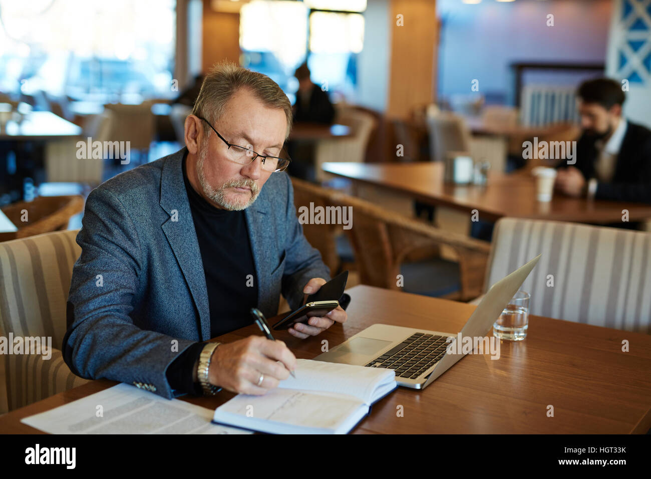 Mature trader with gadgets making notes in his notebook Stock Photo - Alamy